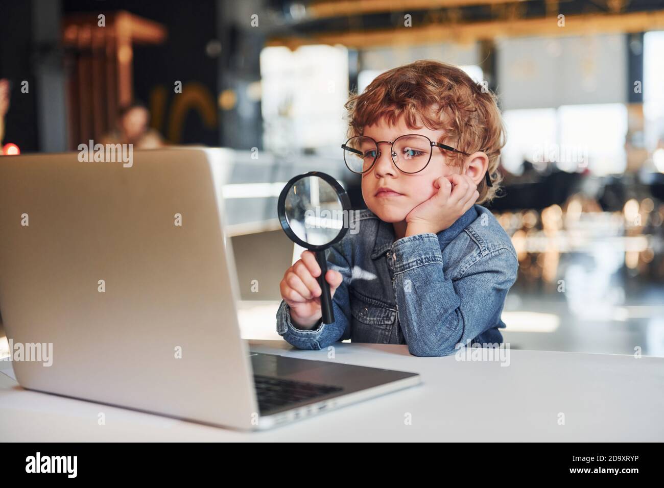 Smart child in casual clothes and in glasses using laptop for education ...