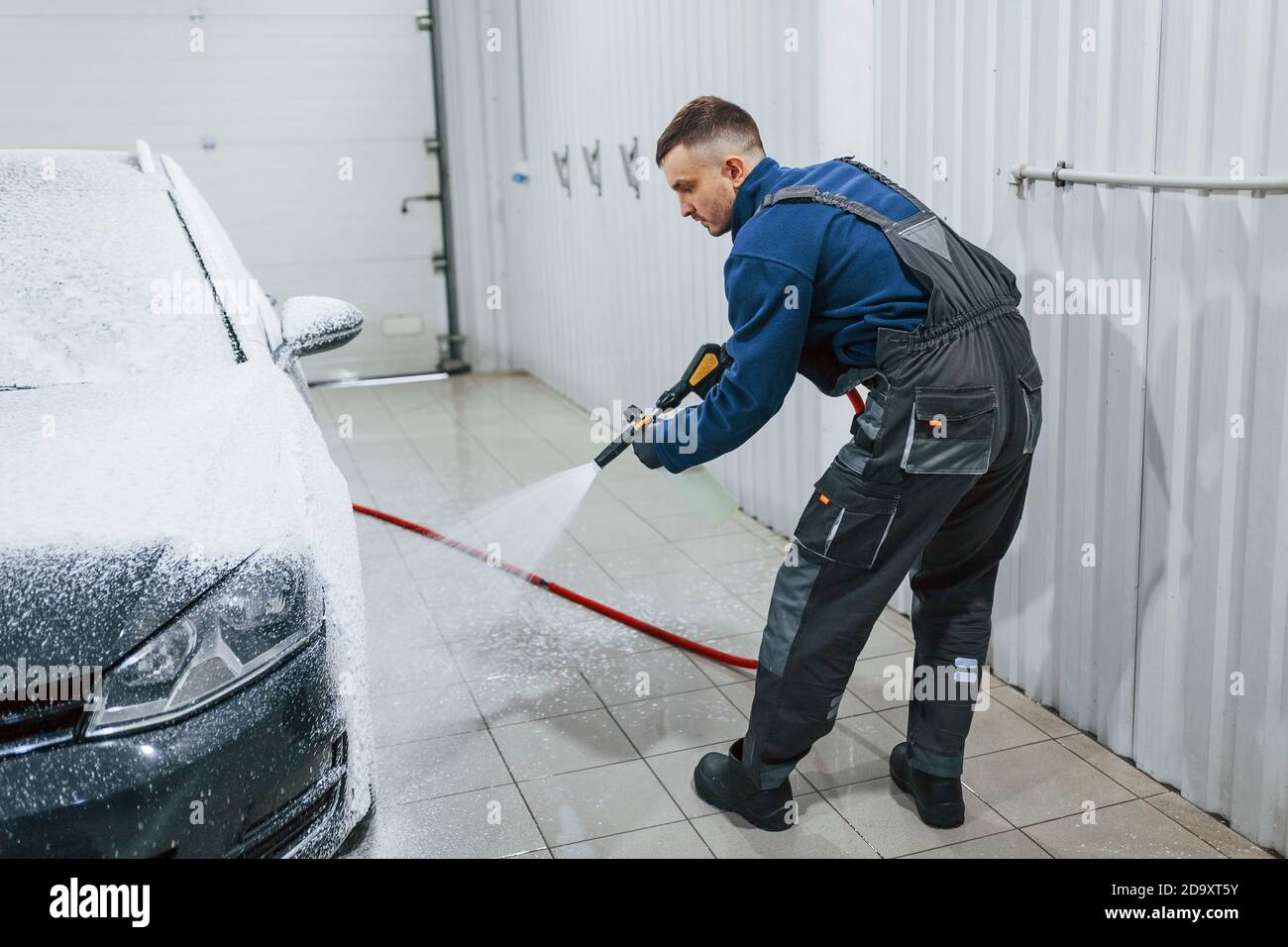 Male worker in uniform washing new modern car that covered with soap ...