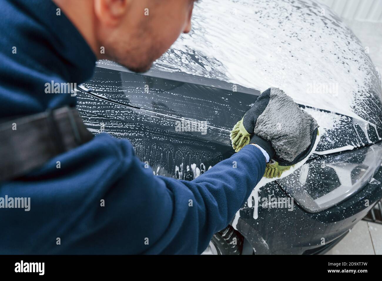 Male worker in uniform washing new modern car that is full of soap ...