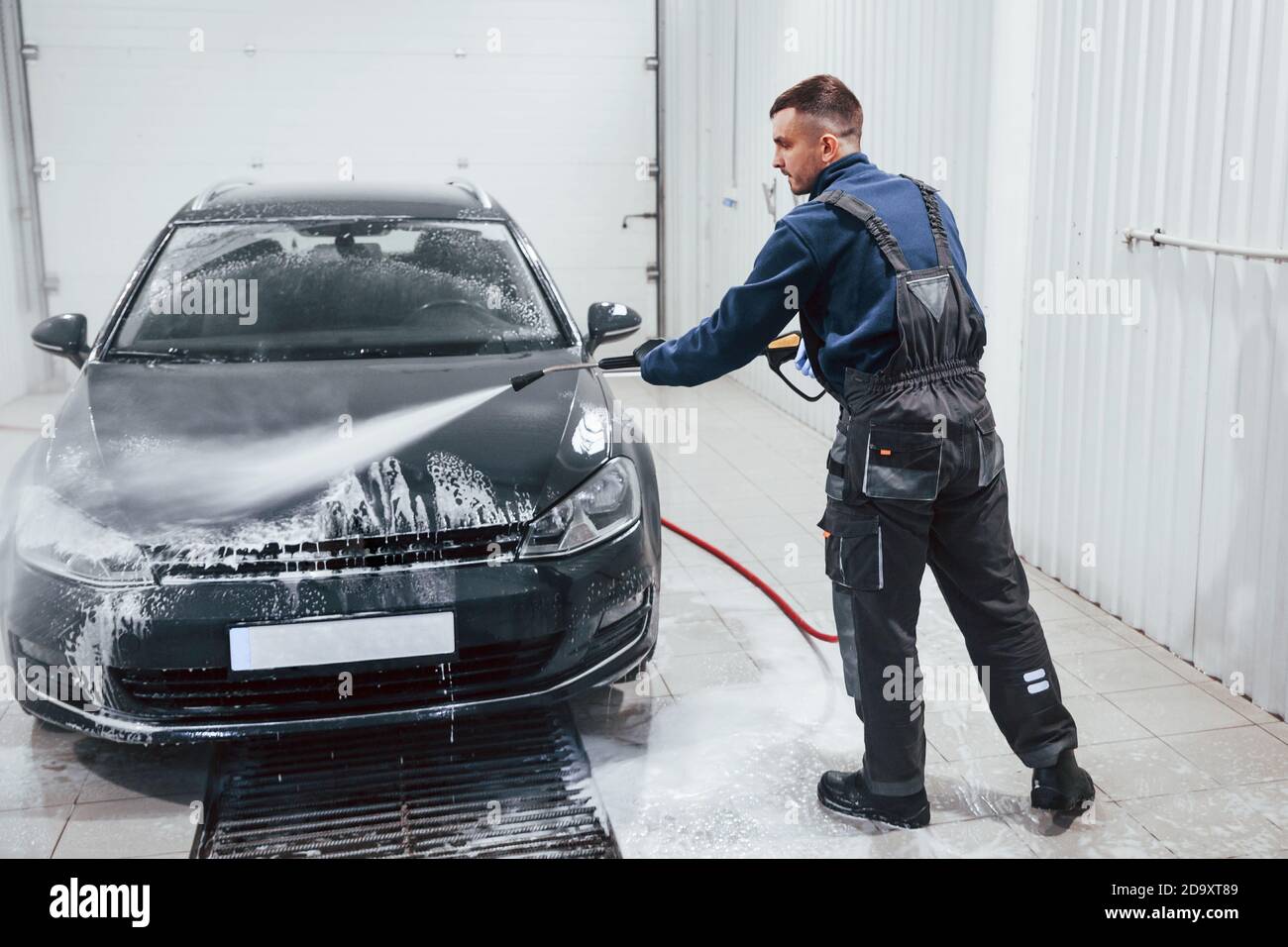 Male worker in uniform washing new modern car that covered with soap ...