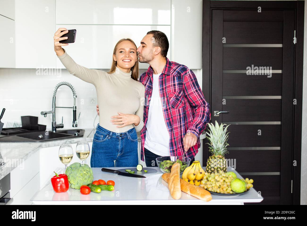 Portrait of smiling young couple taking a selfie while cooking together ...