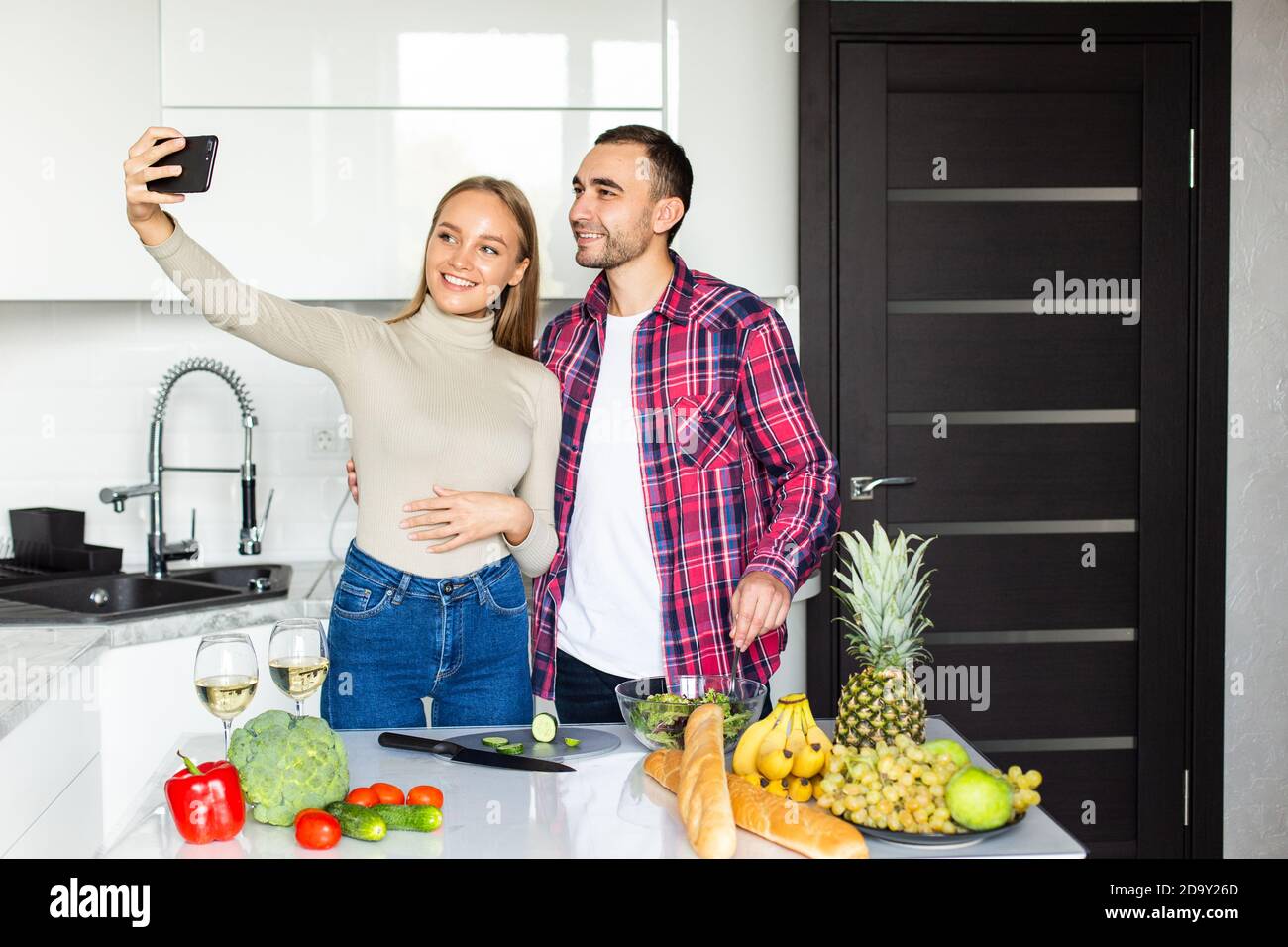 Portrait of smiling young couple taking a selfie while cooking together ...