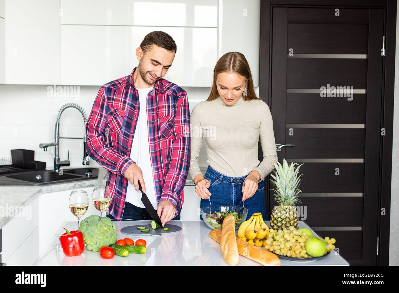 Beautiful young couple is talking while cooking healthy food in kitchen ...