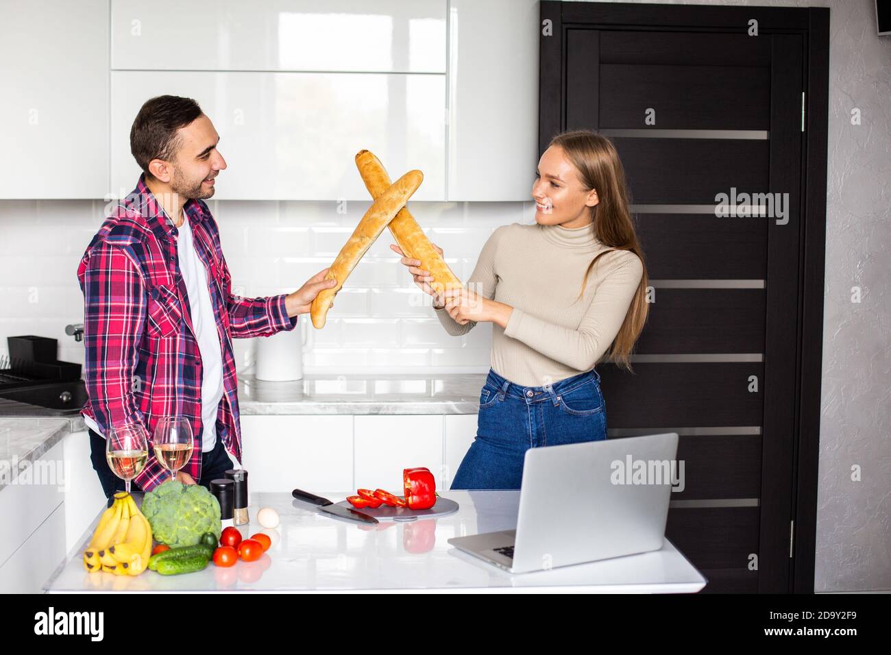 Attractive couple having fun in the kitchen fencing with ladle and ...