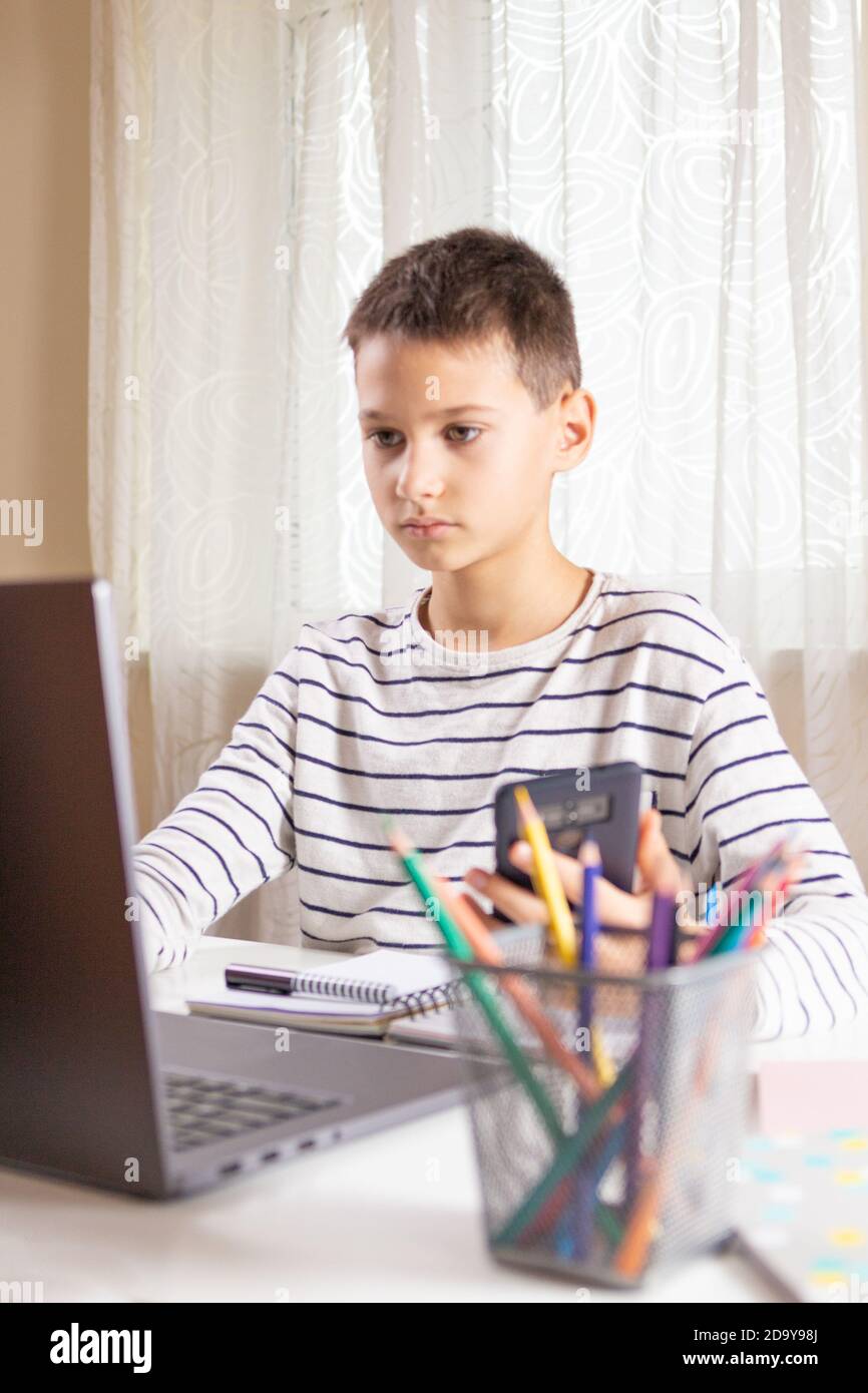 Kid sitting with laptop computer and scrolling phone instead of doing ...