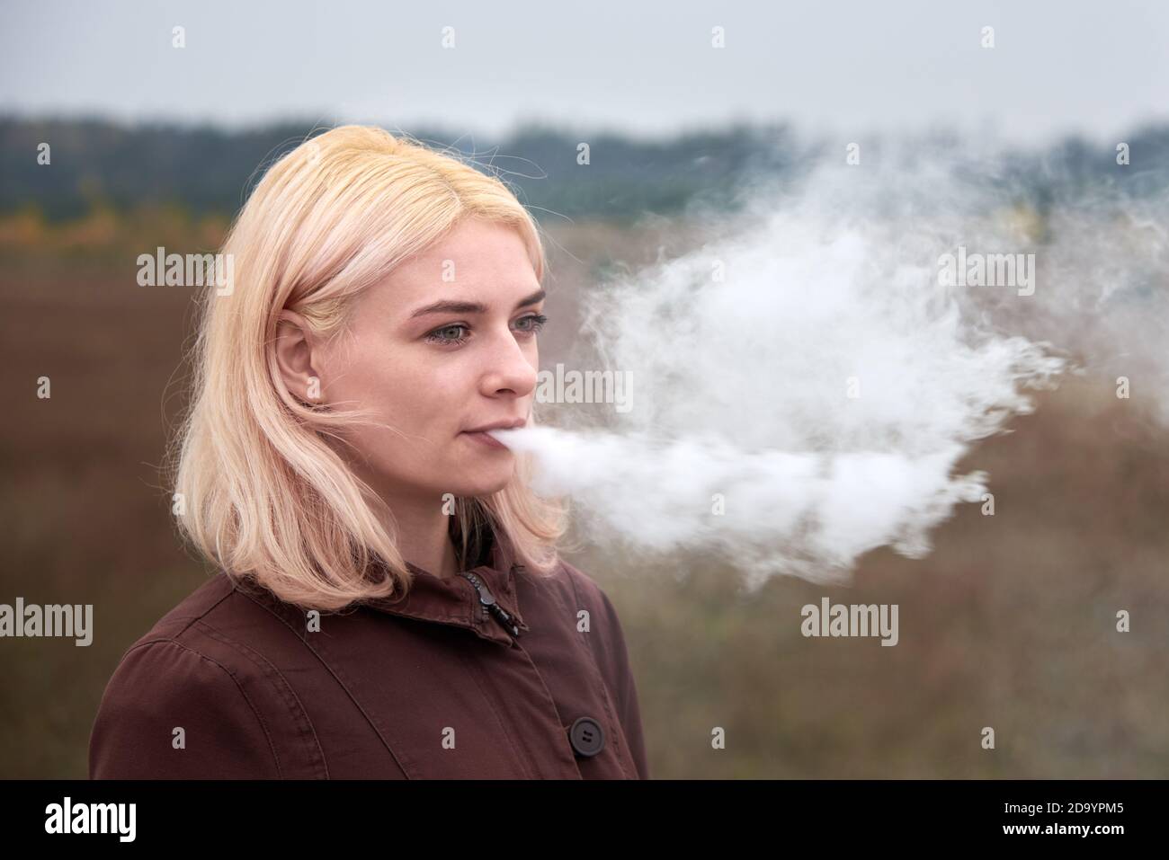 Young blonde woman exhales cigarette smoke on nature in autumn Stock ...