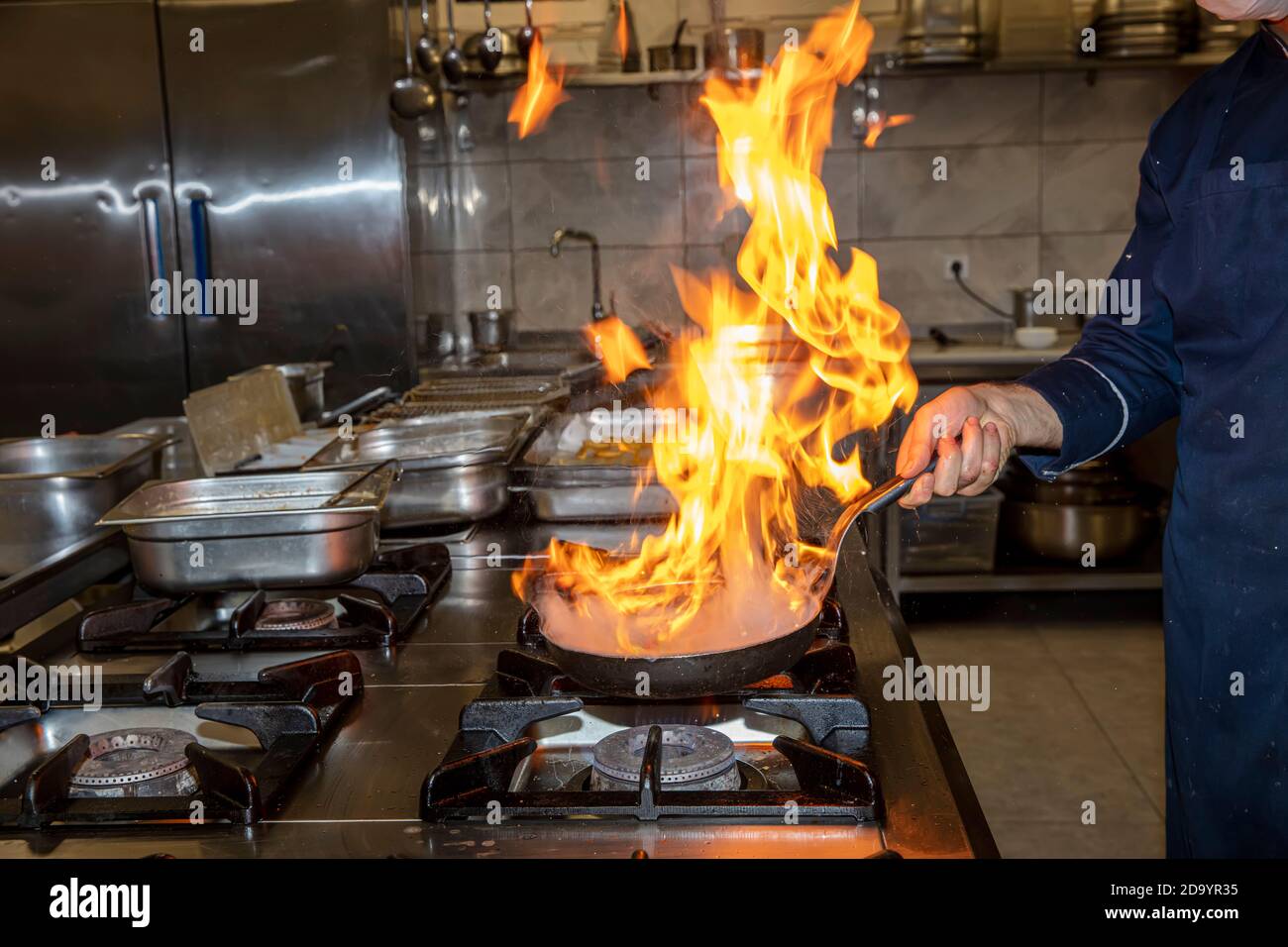 Flame in the pan. Professional Chef makes flambe for food in the ...