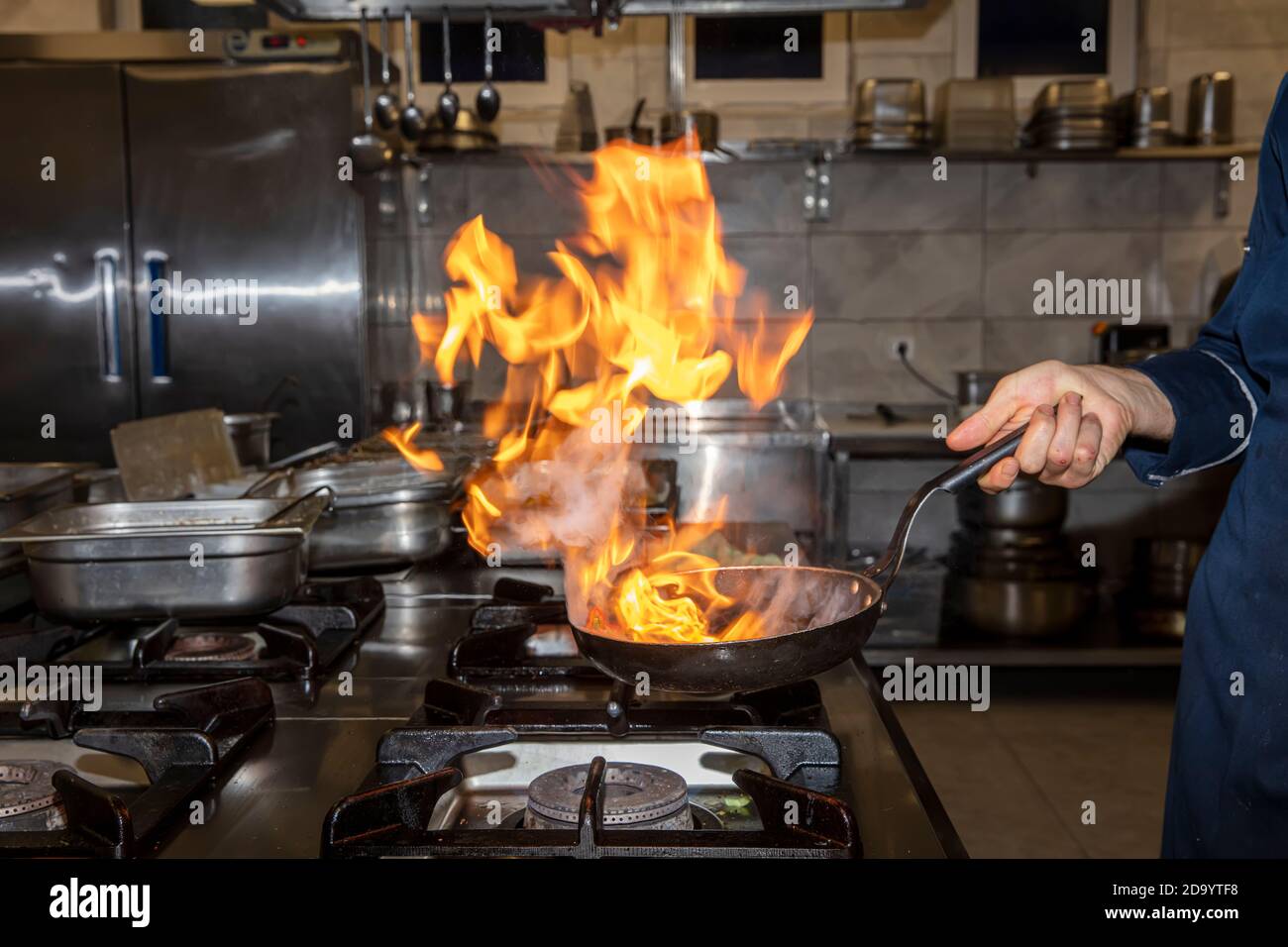 Flame in the pan. Professional Chef makes flambe for food in the ...