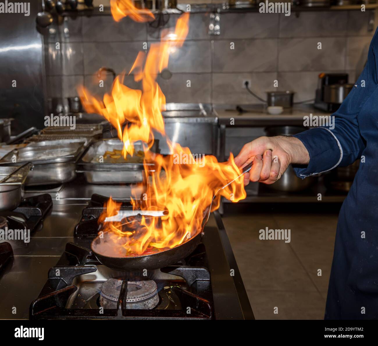 Flame in the pan. Professional Chef makes flambe for food in the ...