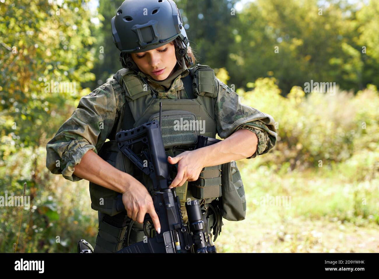 confident soldier woman loading rifle in the forest, alone, looking at ...