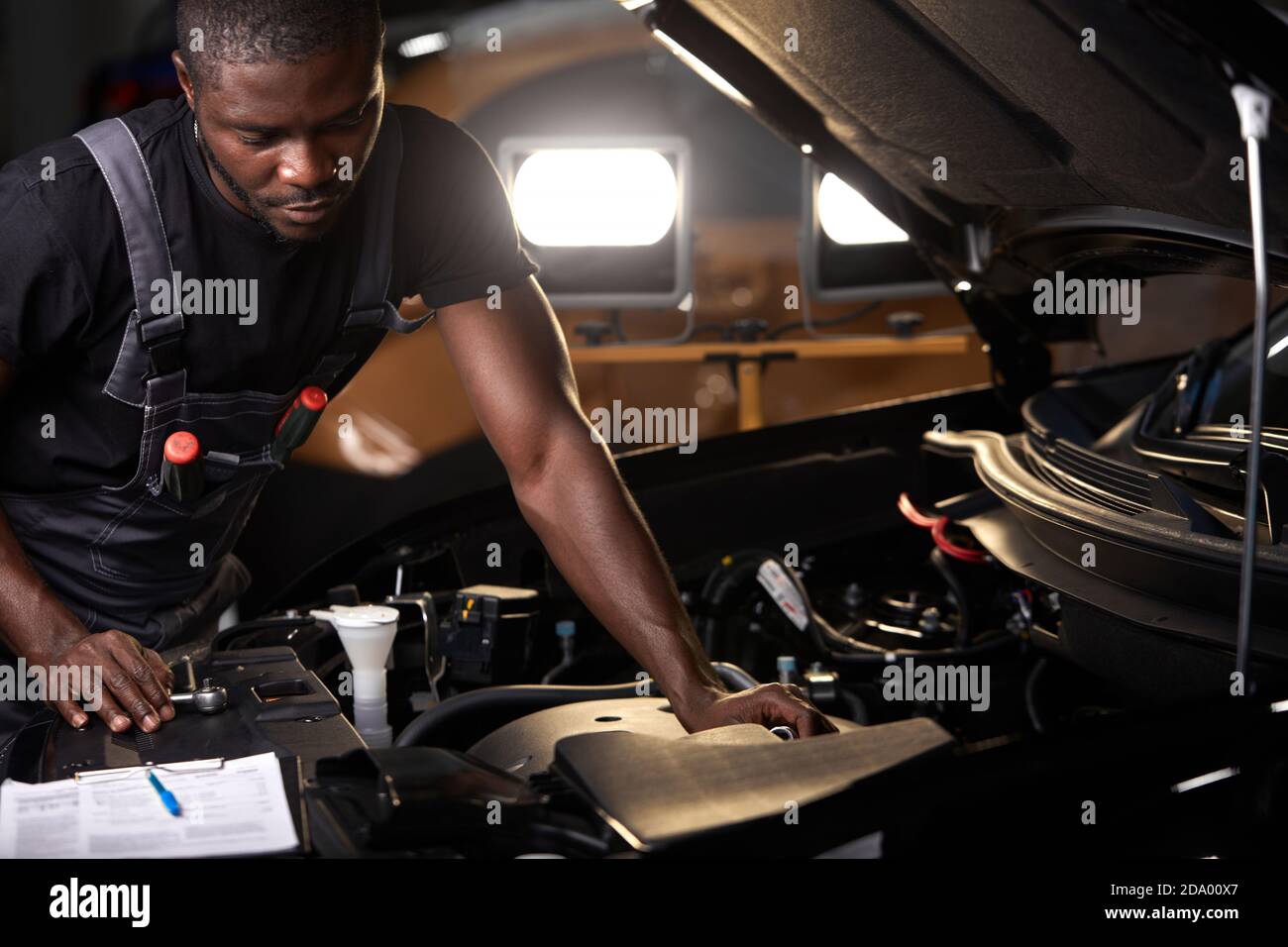 professional car mechanic is examining engine under the hood at auto ...