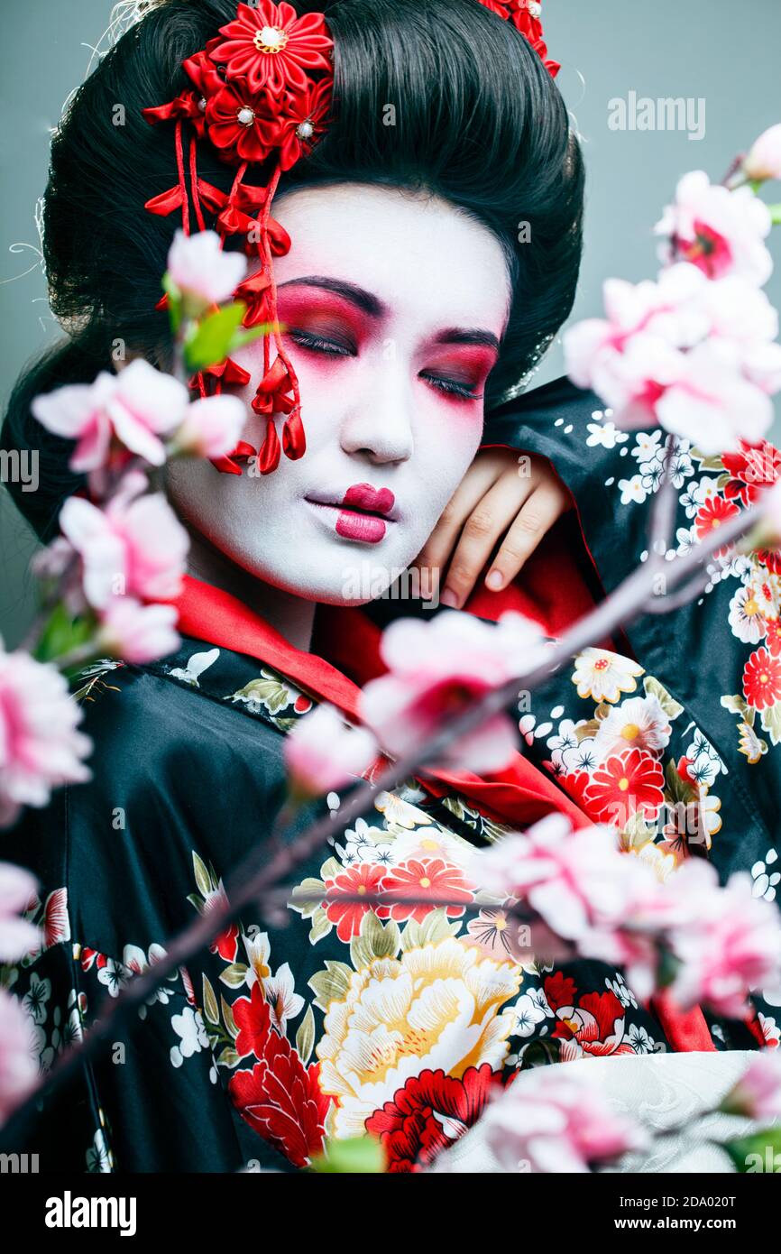 young pretty geisha in black kimono among sakura, asian ethno close up ...