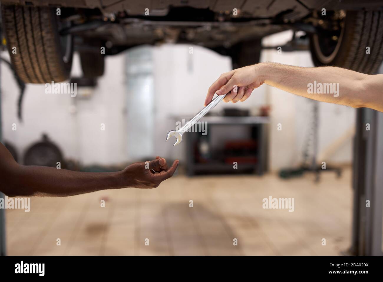 two auto mechanic colleagues giving tools to each other, cropped hands ...