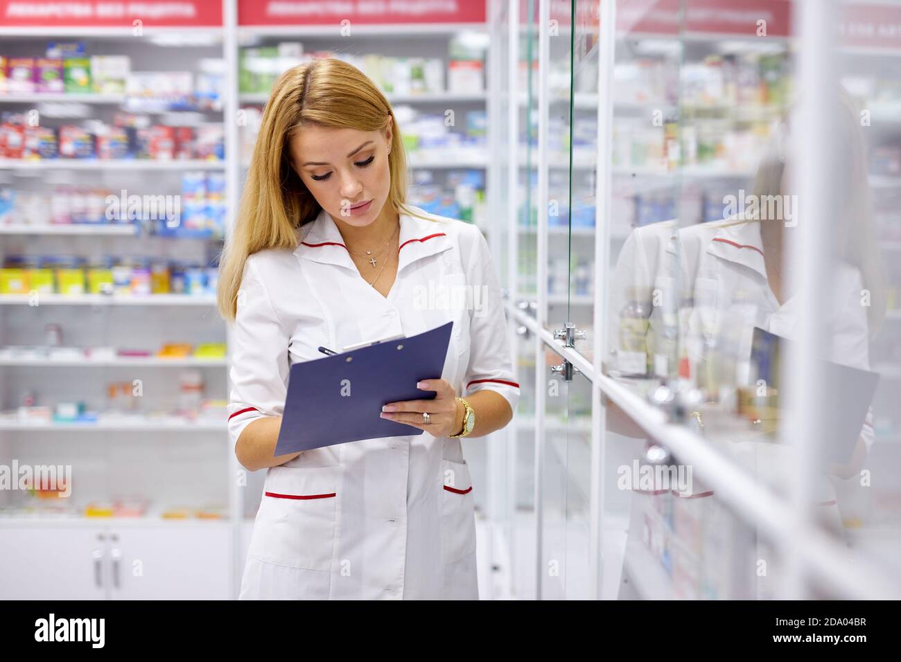 portrait of good-looking blonde pleasant female pharmacist writing on ...
