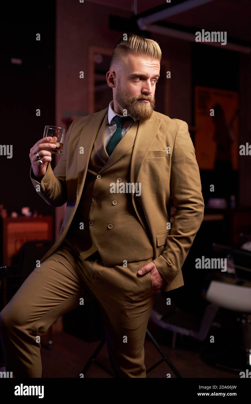 good-looking male in suit drinking alcohol, he holds glass of beverage ...