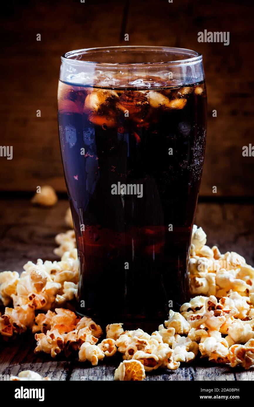 Large glass of cola, salty popcorn spilled on the table, vintage dark ...