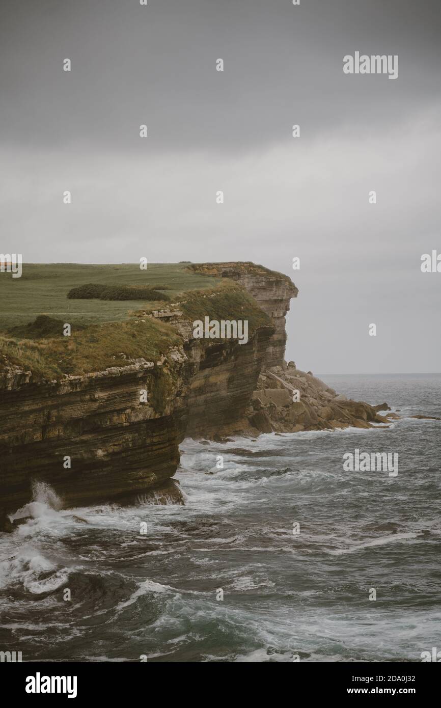 Scenic landscape of rocky cliff near stormy sea under gray sky in ...