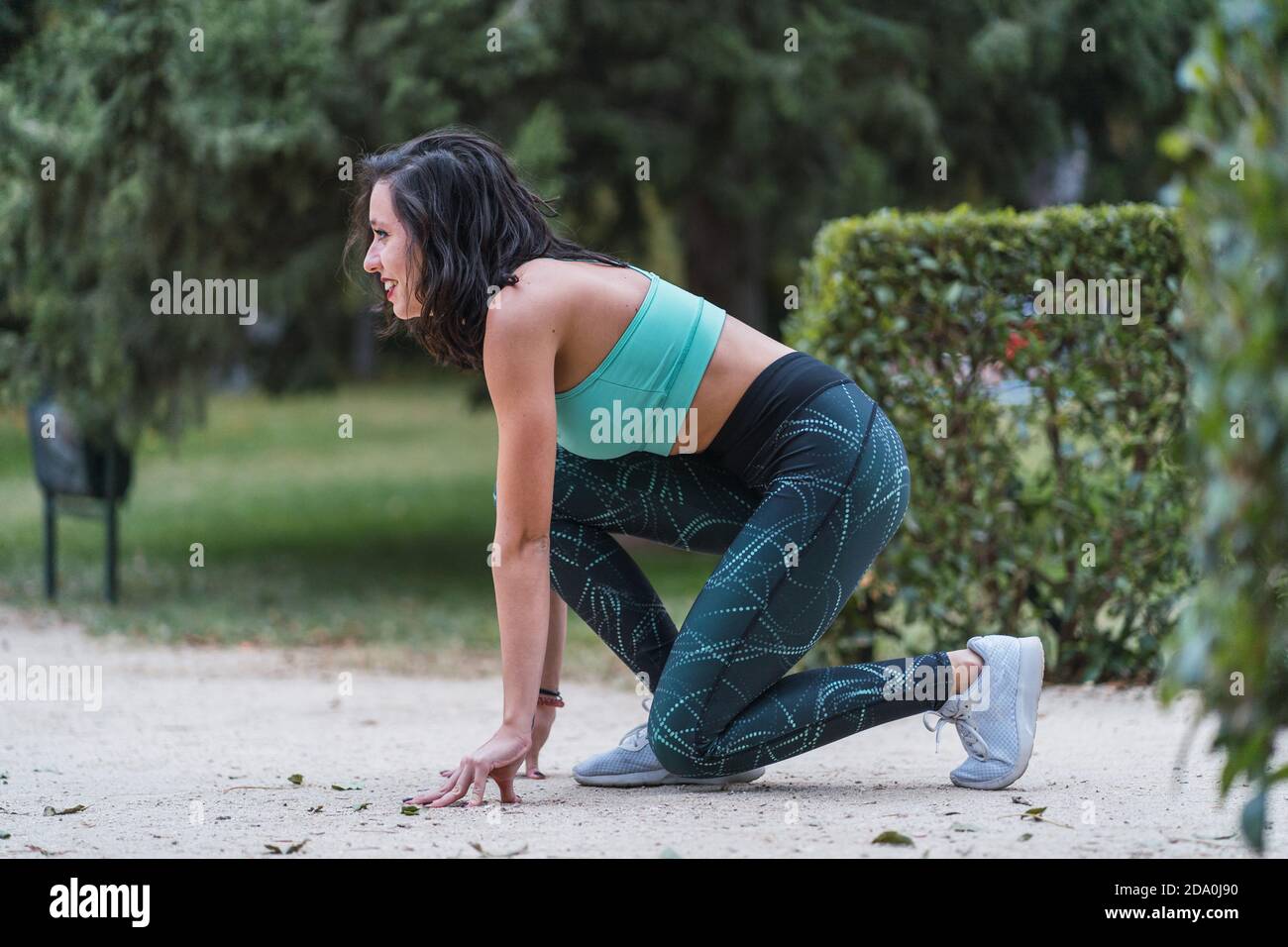 Side view of smiling female runner standing in crouch start position ...