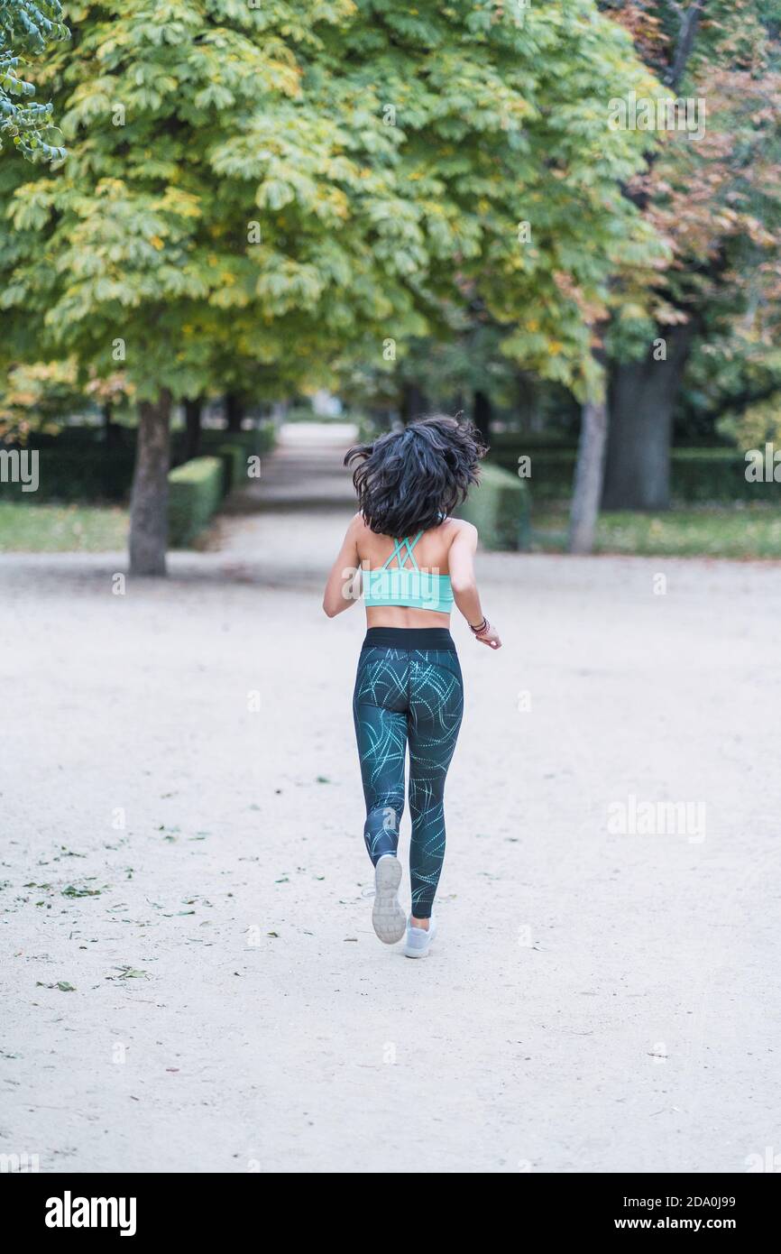 Full body back view of slim female running along path in park while ...