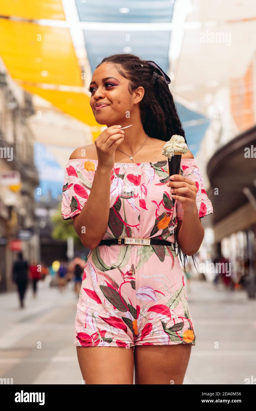 Young content ethnic female in trendy clothes eating delicious ice ...
