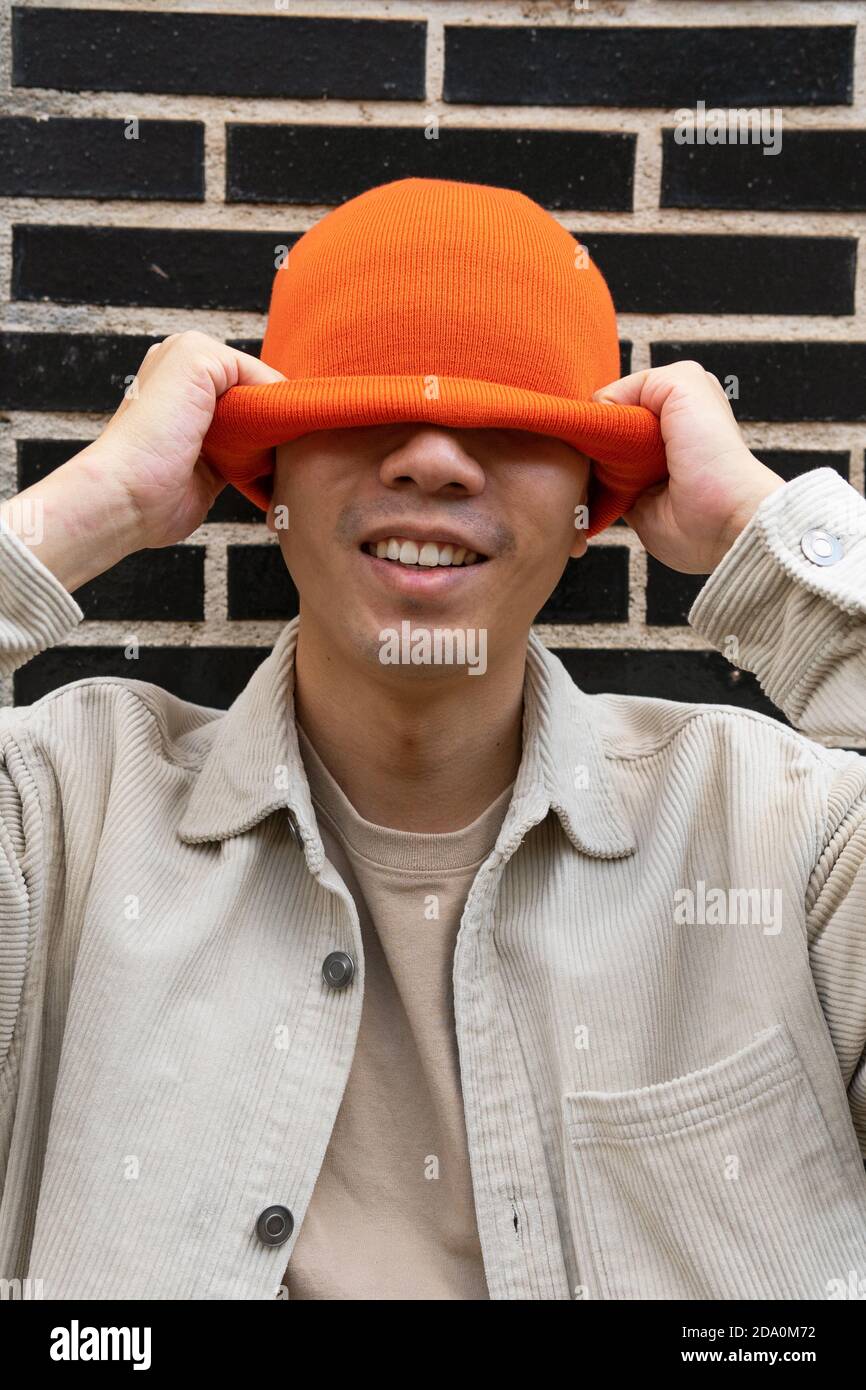 Happy male putting knitted orange hat on head and covering eyes while ...