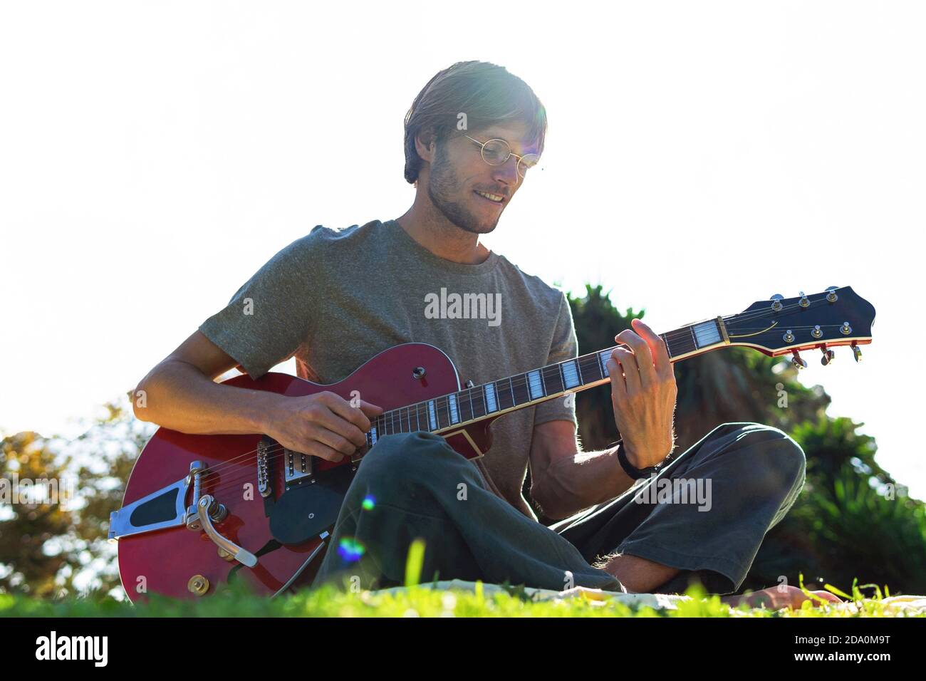 Ground level of smiling male musician sitting on lawn and playing ...