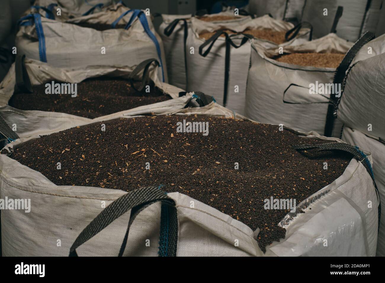Huge bags with black grain crops stored in stock in industrial facility ...