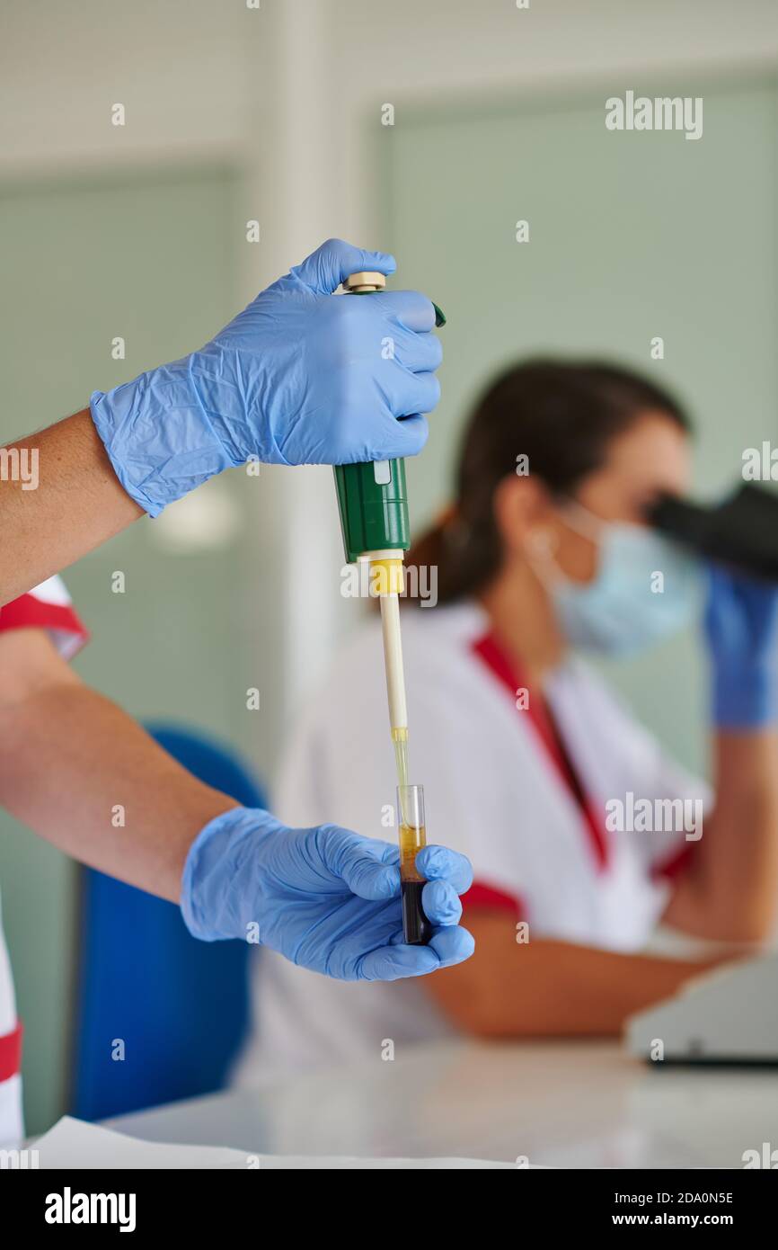 Crop anonymous medical specialist filling sample tube with blood while ...