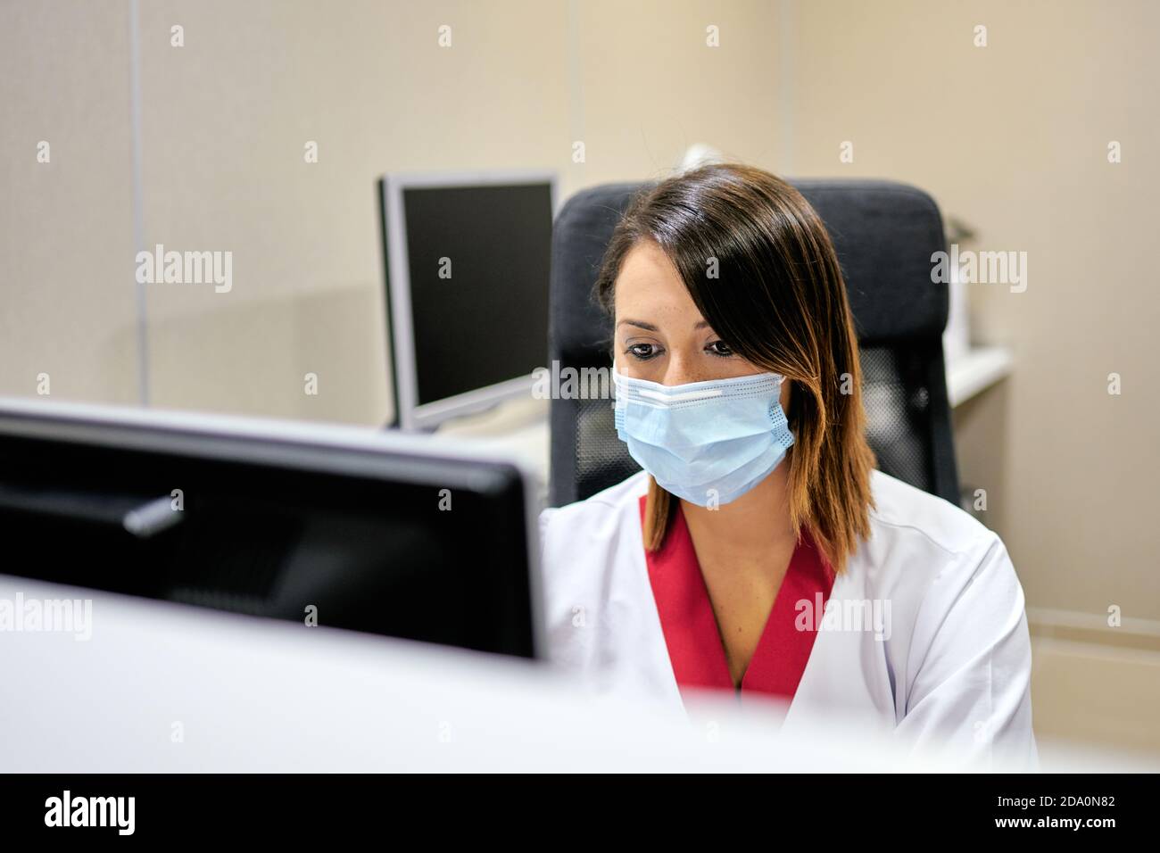 Calm female hospital administrator in medical robe and mask using ...