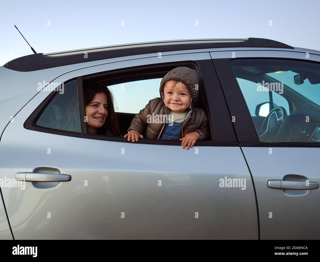 Cheerful cute toddler peering out of car window while sitting on back ...
