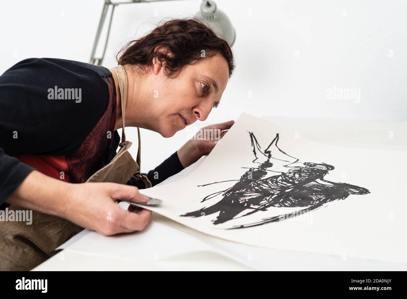 Side view of artisan female printmaker examining paper sheet with ...