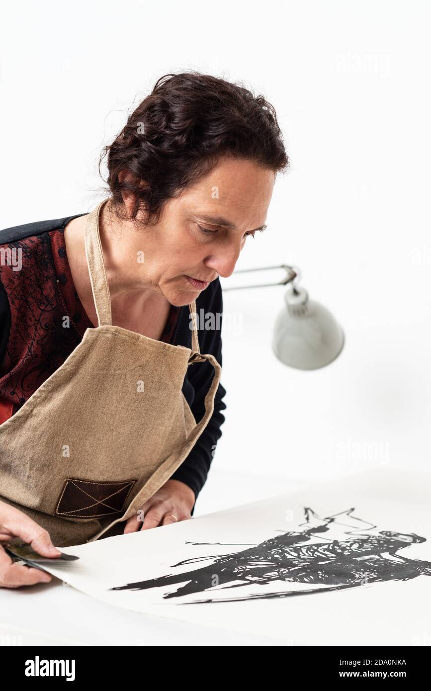 Side view of artisan female printmaker examining paper sheet with ...