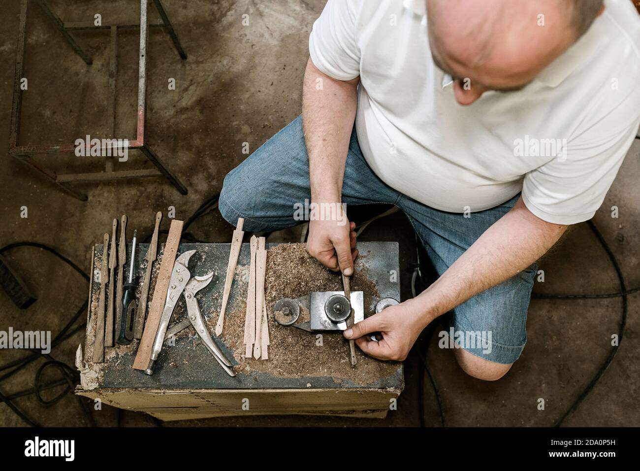 From above of anonymous male carpenter grinding wooden details while ...
