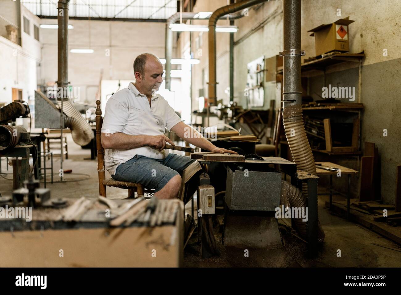 Determined male woodworker sitting at old workbench and working with ...