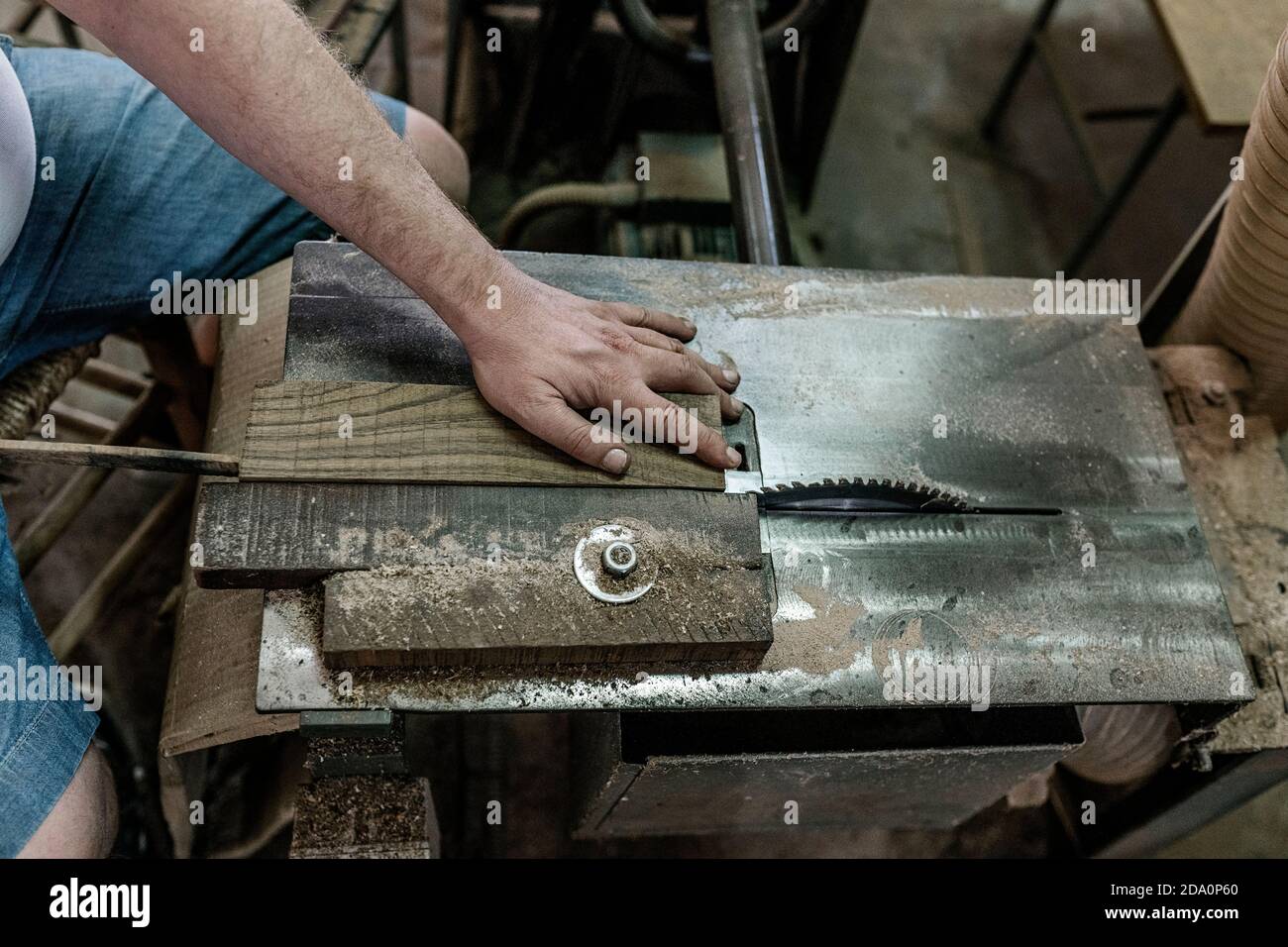 High angle of male carpenter sitting at workbench and cutting piece of ...