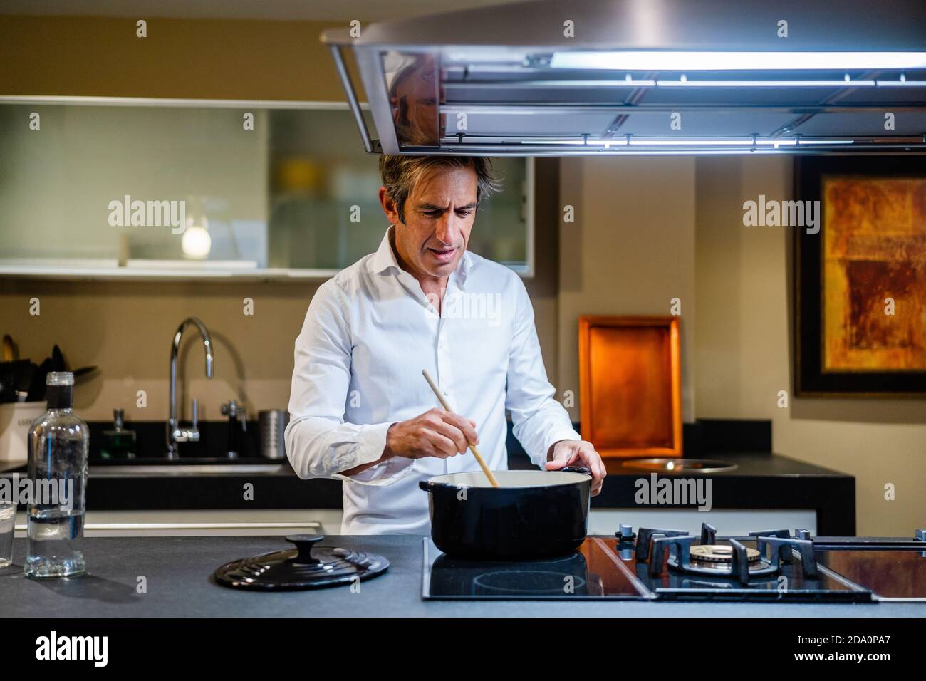 Cheerful middle age male cooking dinner in modern kitchen with bright ...