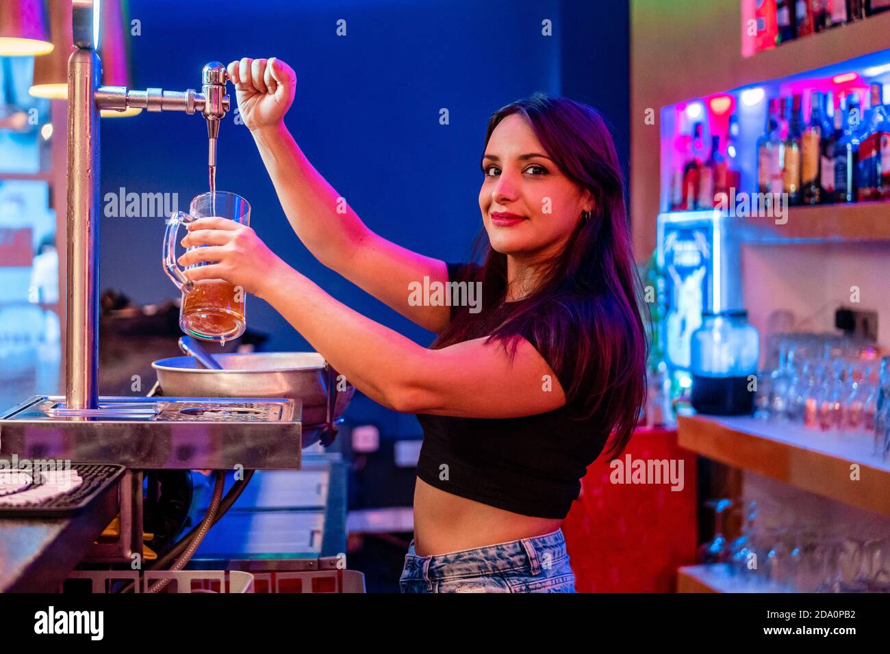 Side view of happy young female barkeeper pouring beer into glass while ...