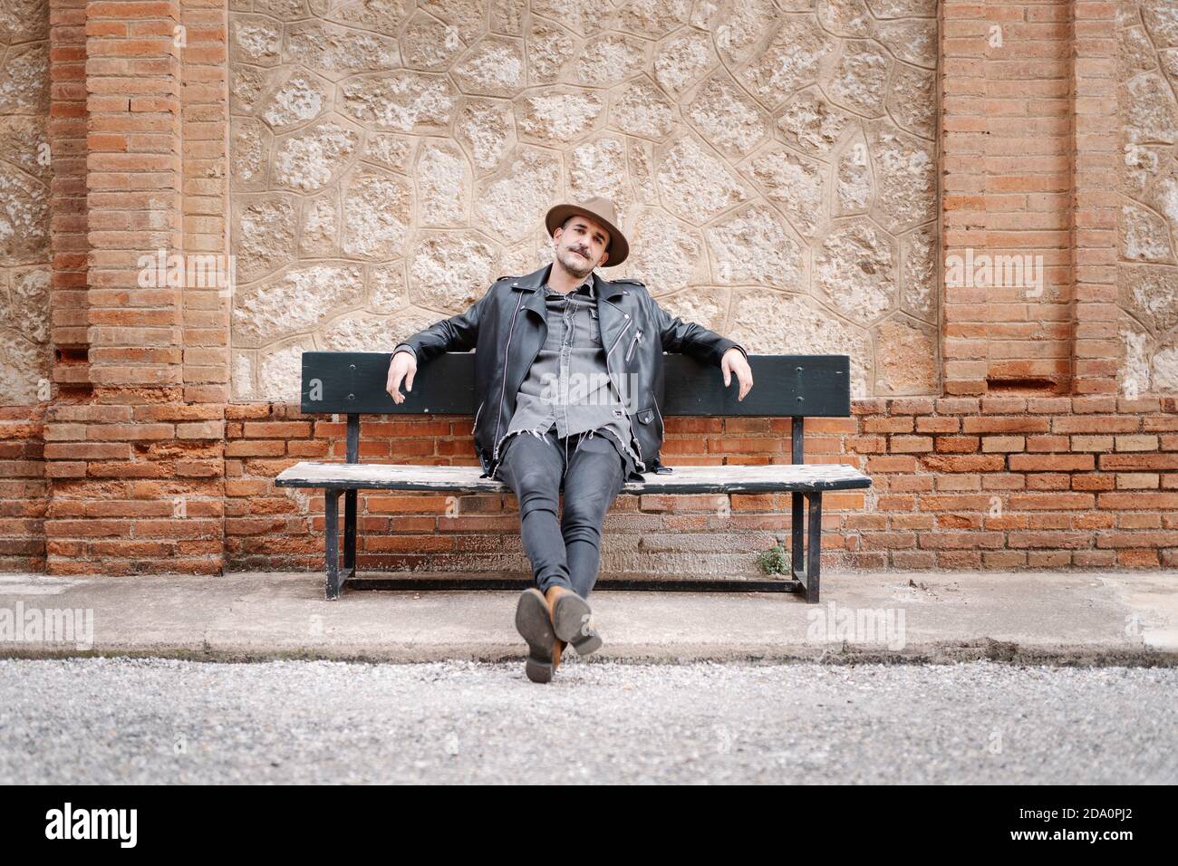 Serious male with mustache wearing hat and leather jacket relaxing on ...
