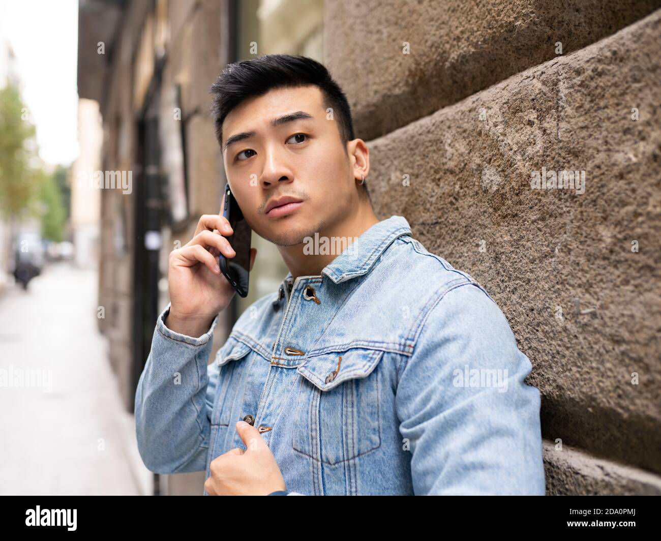 Serious young Asian male in casual outfit speaking on mobile phone ...
