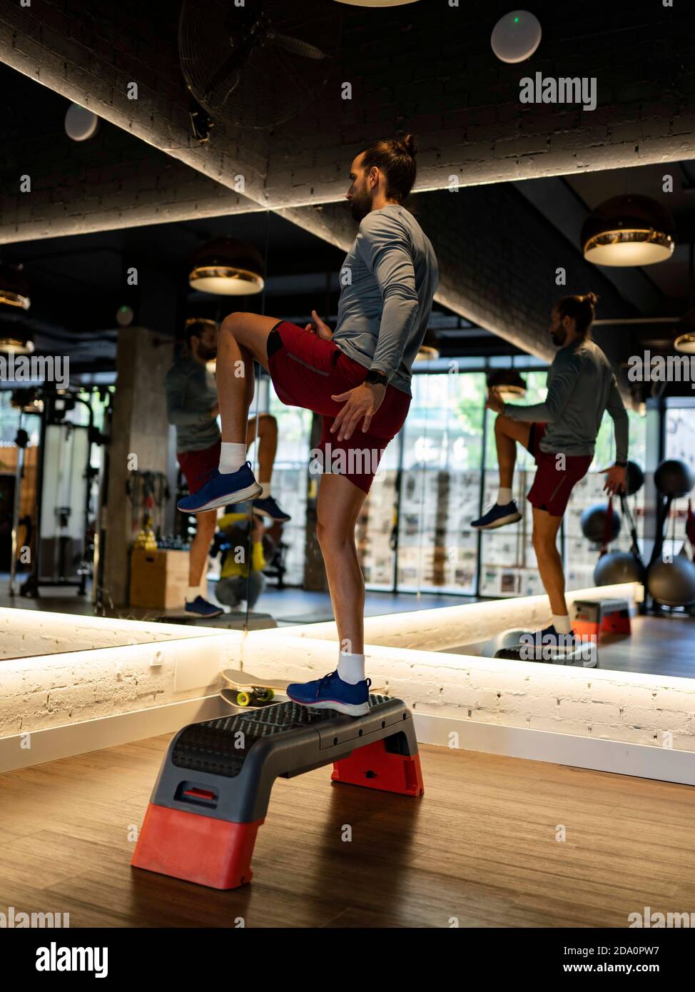 Full body male athlete standing on step and lifting leg near mirror ...