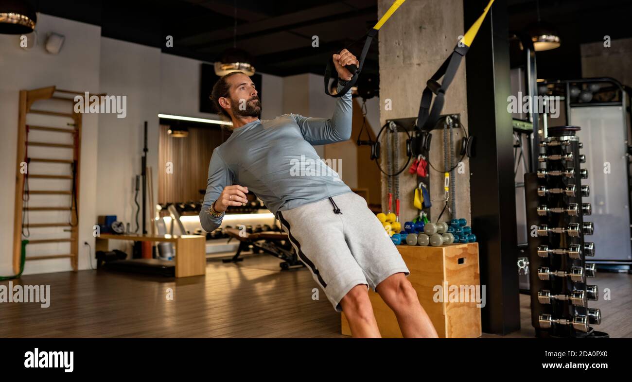 Side view of concentrated muscular male athlete practicing suspension ...