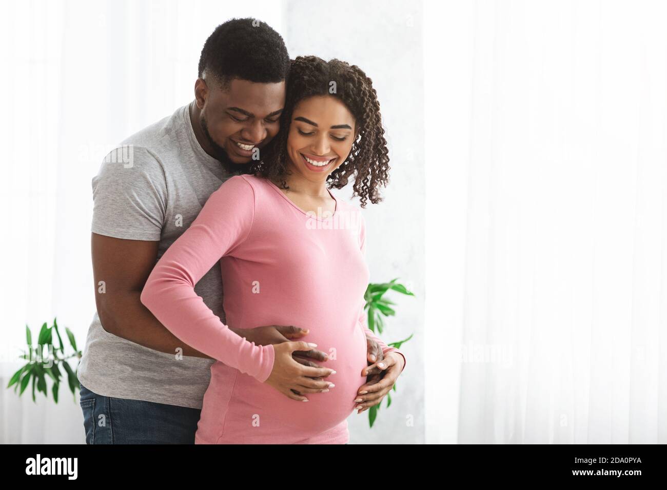 Loving pregnant couple cuddling while spending time at home Stock Photo ...