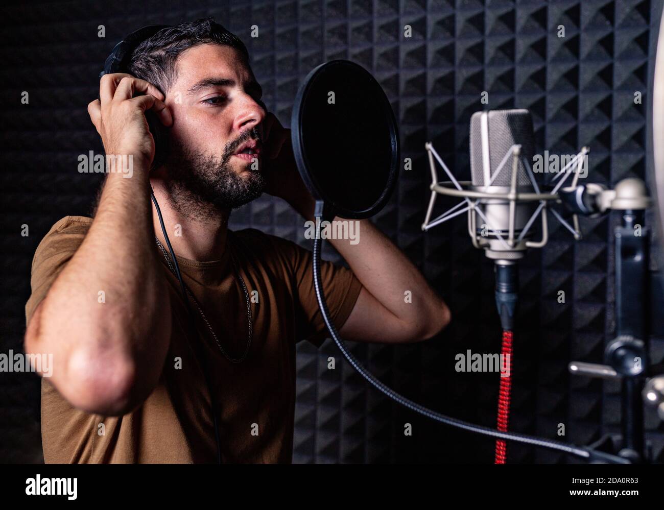 Side view of male singer in headphones standing in acoustic room with ...