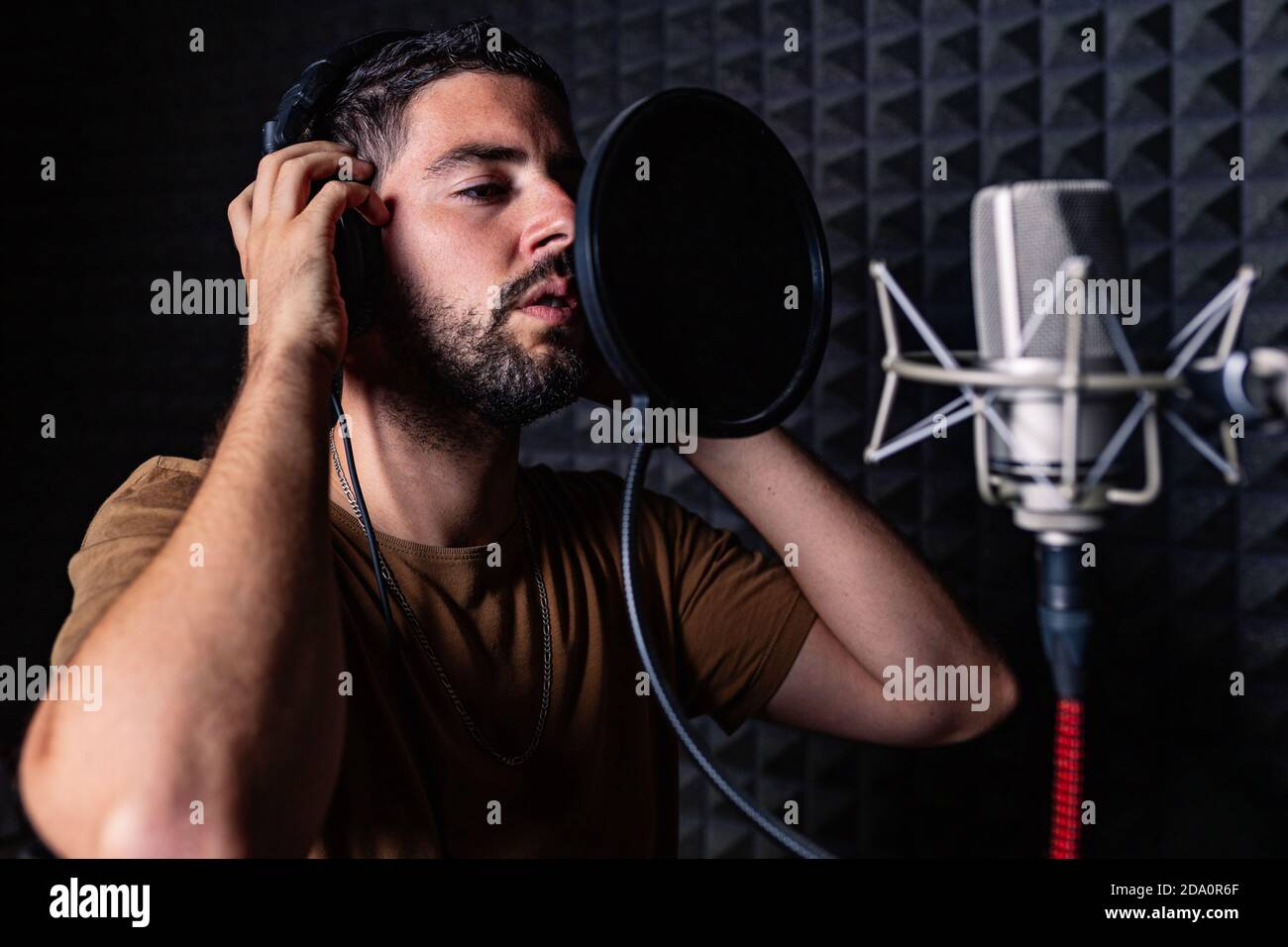 Side view of male singer in headphones standing in acoustic room with ...