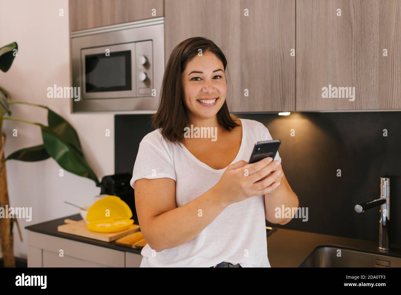 Happy and smiley brunette Woman with smartphone in the kitchen Stock ...