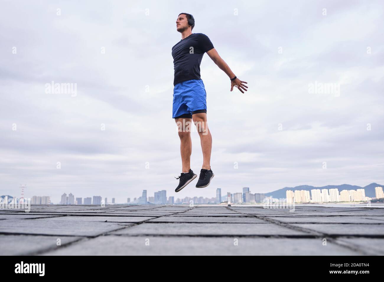 Ground level of energetic male runner warming up body and jumping on ...