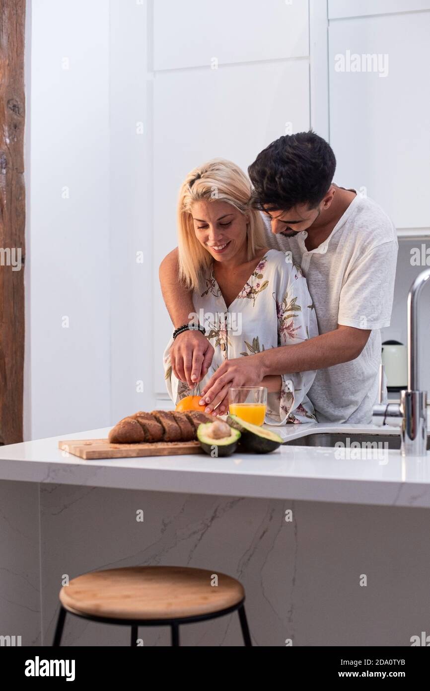 Playful couple eating oranges in kitchen together while hugging and ...