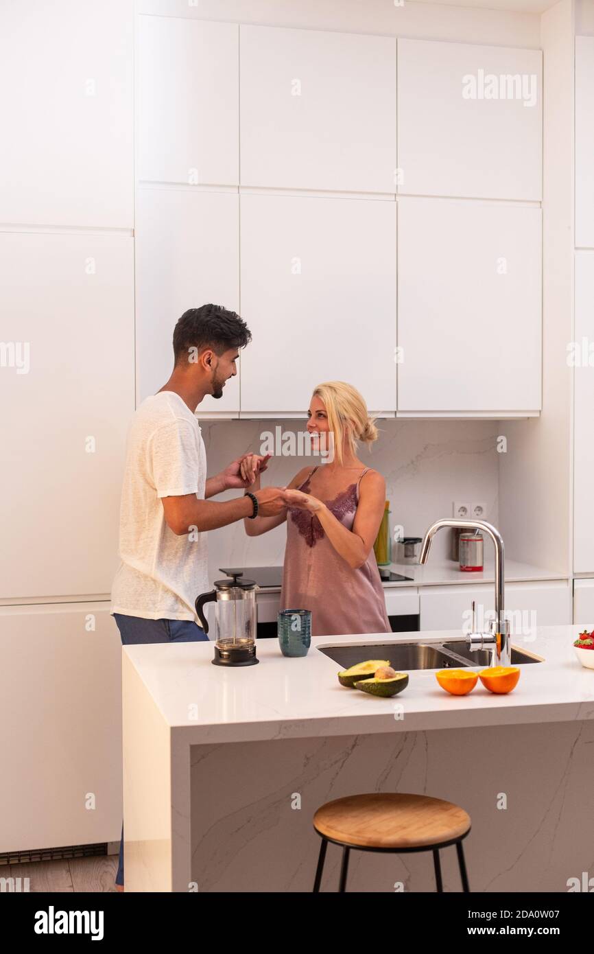 Side view of smiling couple cuddling in modern kitchen during breakfast ...