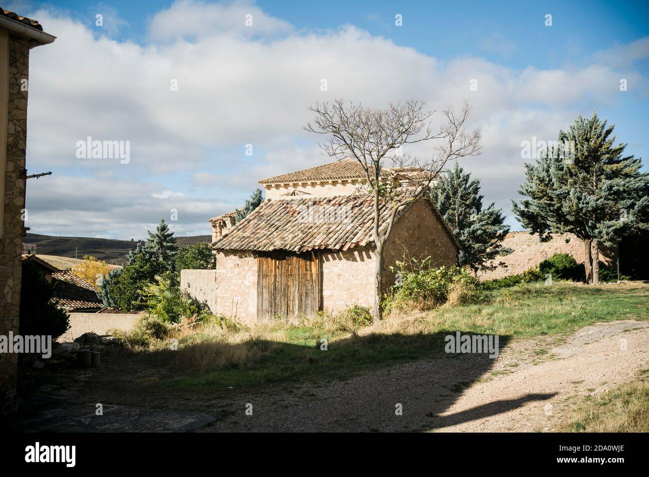 Weathered stone building with shabby tiled roof and dried leafless tree ...