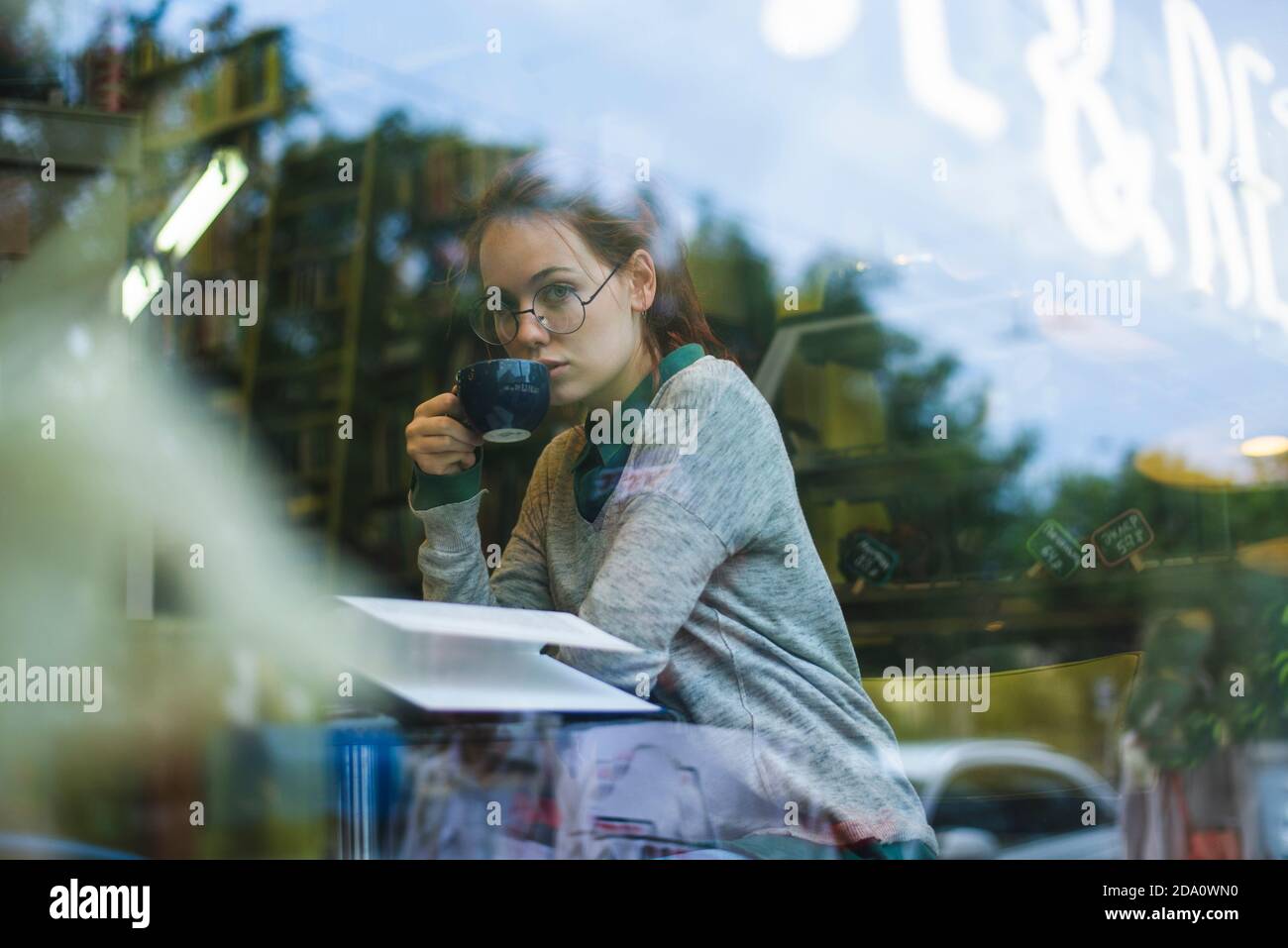 Through glass side view of relaxed female in casual outfit sitting at ...